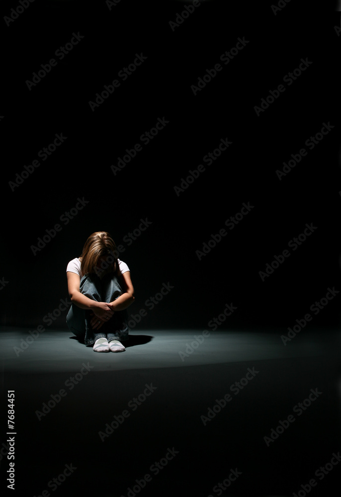 Woman sitting with her knees up and head down. Stock Photo | Adobe Stock