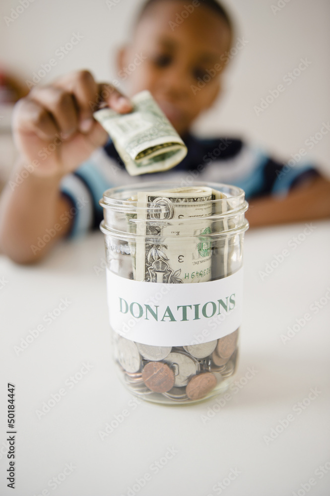 Black boy putting money into donations jar Stock Photo | Adobe Stock