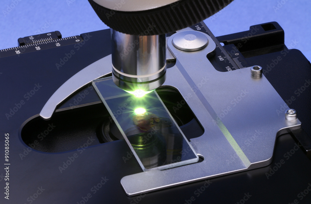 Shiny metal objective and the drop of a liquid illuminated from below ...