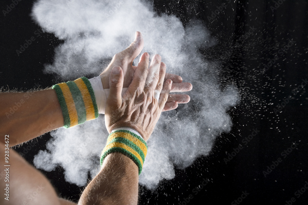 Taped hands of gymnast clapping white chalk powder into a cloud against ...