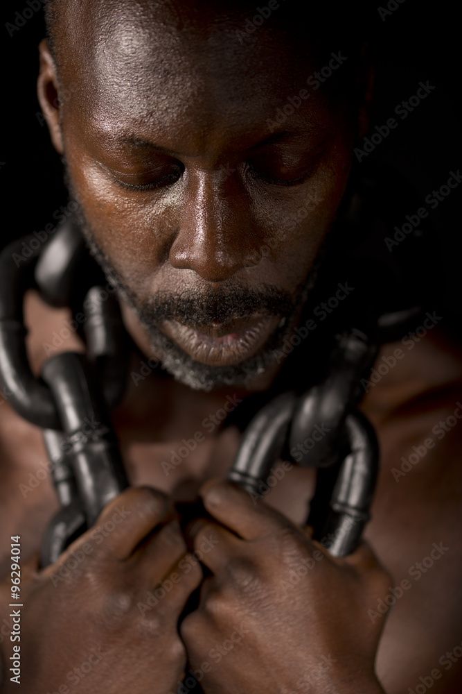 Black man with head bowed, holding large heavy chains around his neck ...