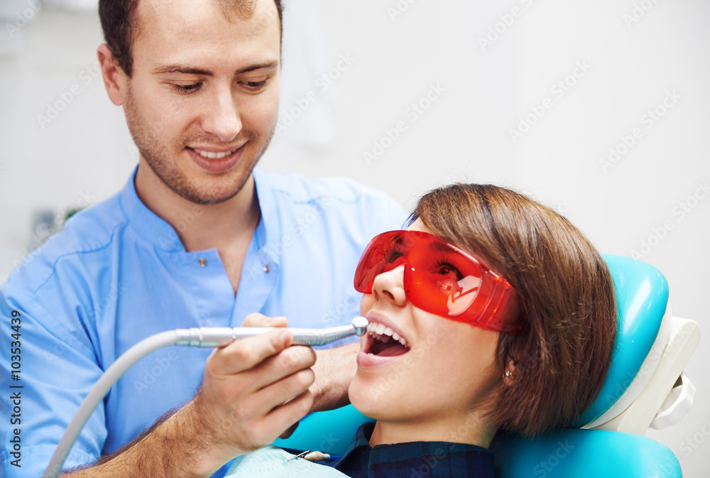Smiling doctor with dental drill curing patient's toothache in hospital ...