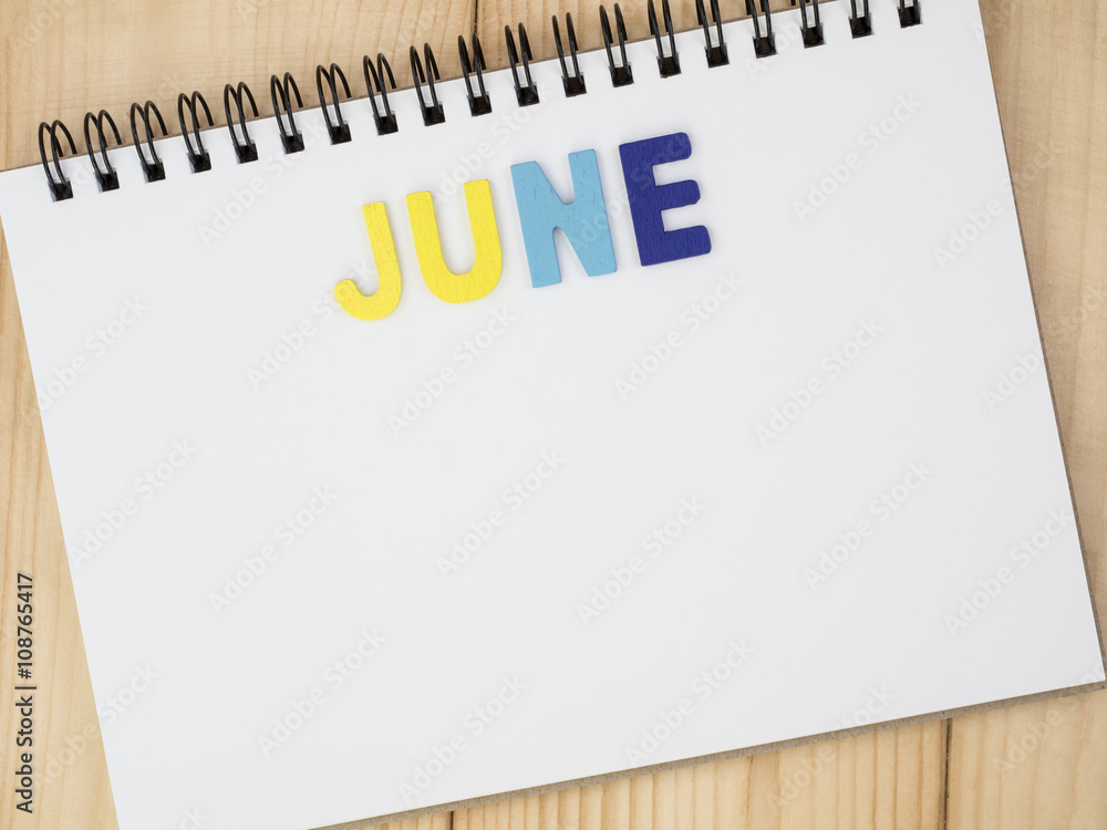 Word spelling month in the year June by wooden letters on notebook with ...