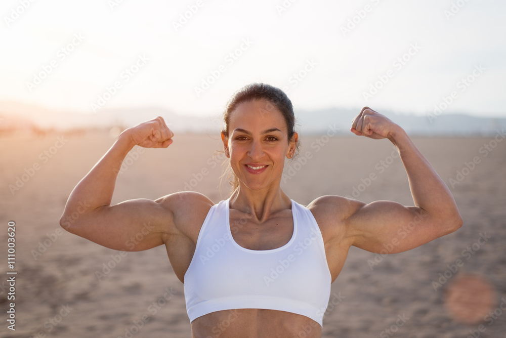 Young fitness woman flexing big strong biceps muscles towards the sun ...