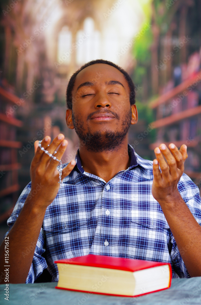 Religious man sitting down holding hands out praying with eyes clsoed ...
