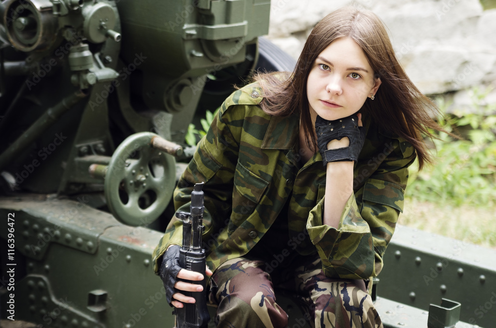 Girl in uniform with a submachine gun sitting on an artillery gun ...