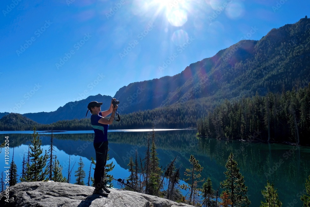 Woman photographer by alpine lake with reflection in calm water. Snow ...
