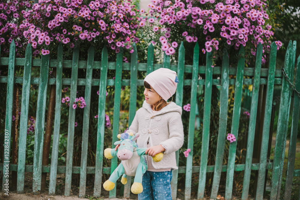 Little (young) girl standing near the green fence and purple flo Stock ...