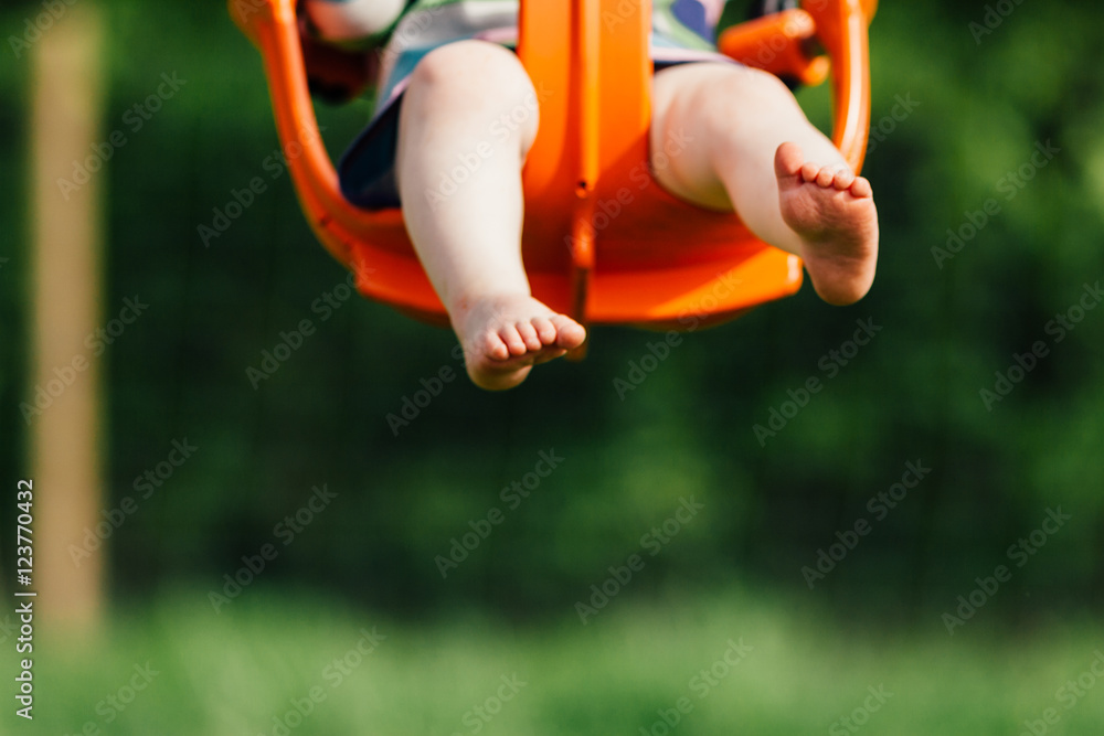 Focus on toddler girl's feet and legs as she swings in an orange baby ...