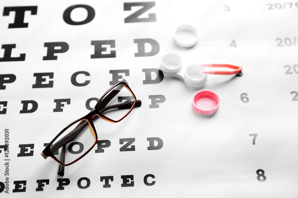 Glasses, lenses container and pincer on eye test chart, close up view ...