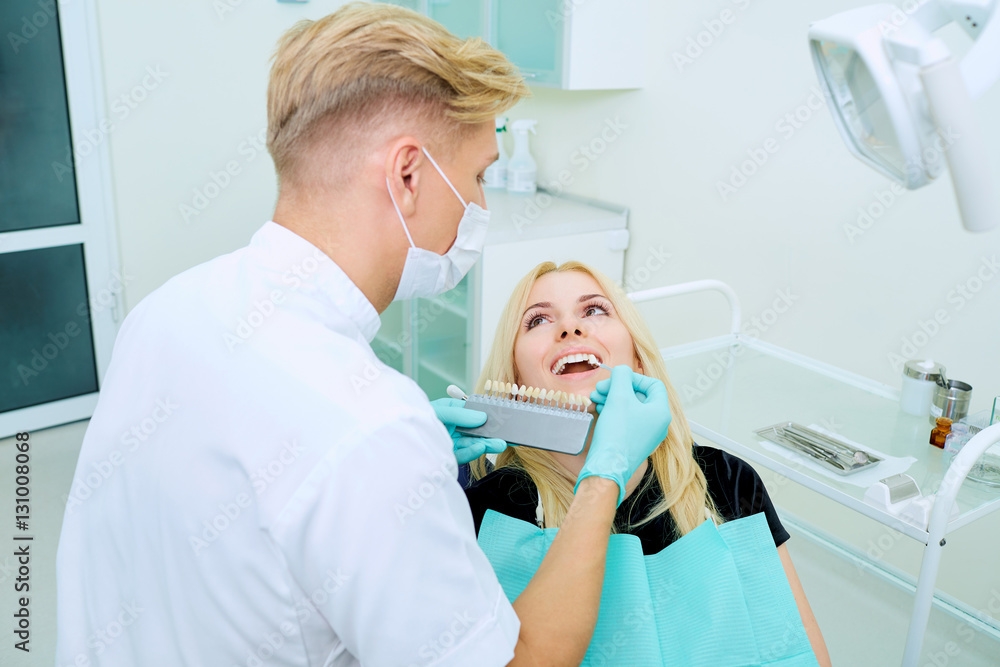 Dentist tries to choose the color of teeth and client in office clinic ...