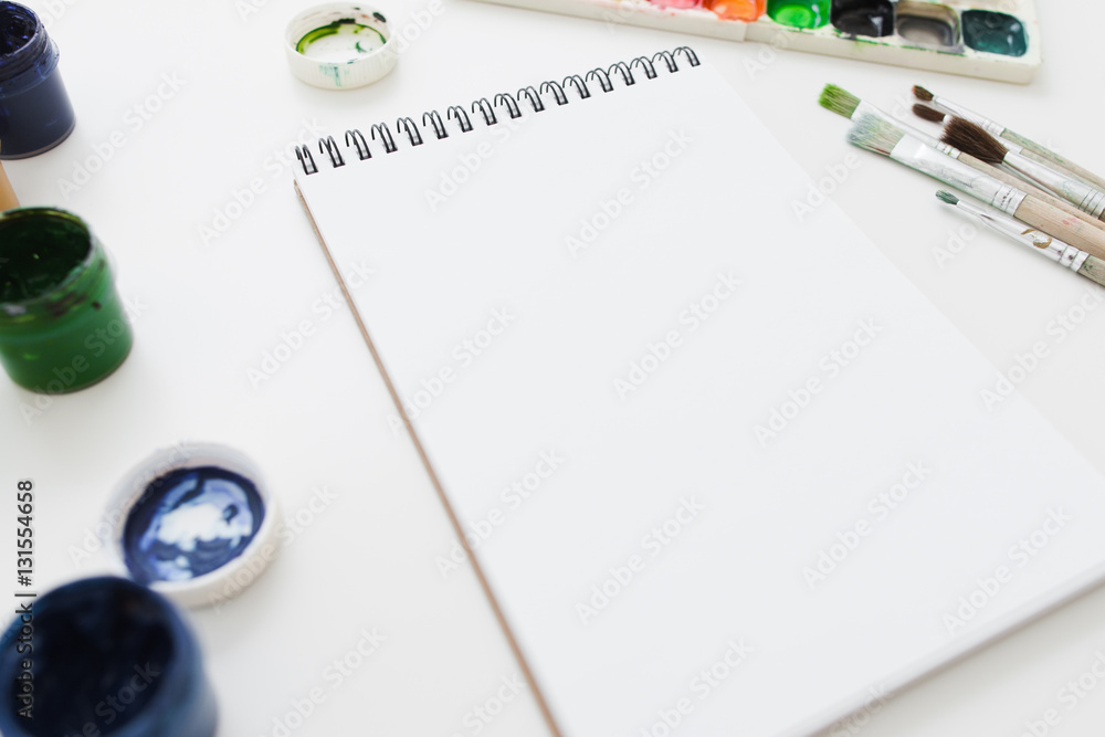 ภาพถ่าย Stock Blank sketchbook with paints and brushes, mockup. Artist workplace with empty ...
