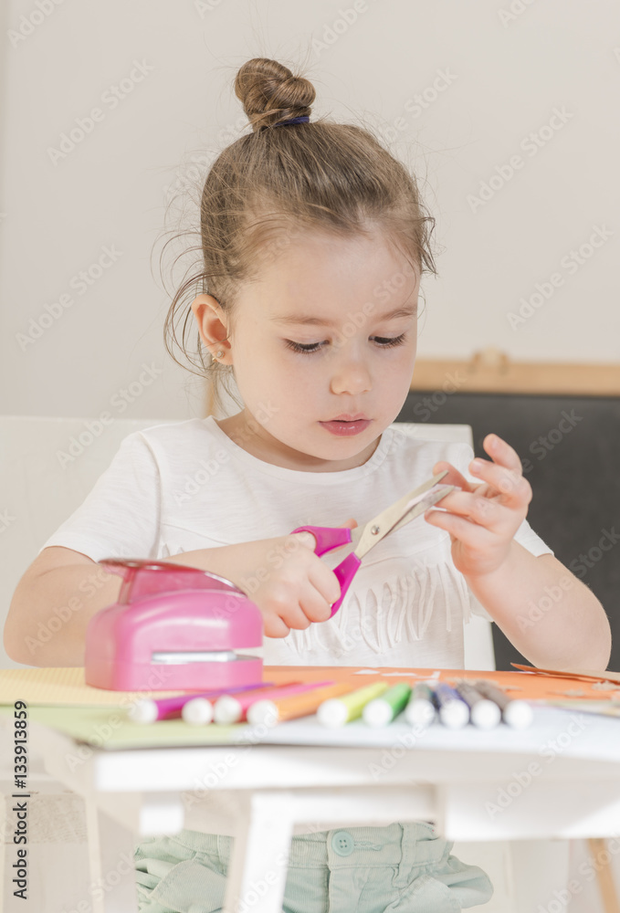 Beautiful little girl cutting paper with scissors on the art lesson ...