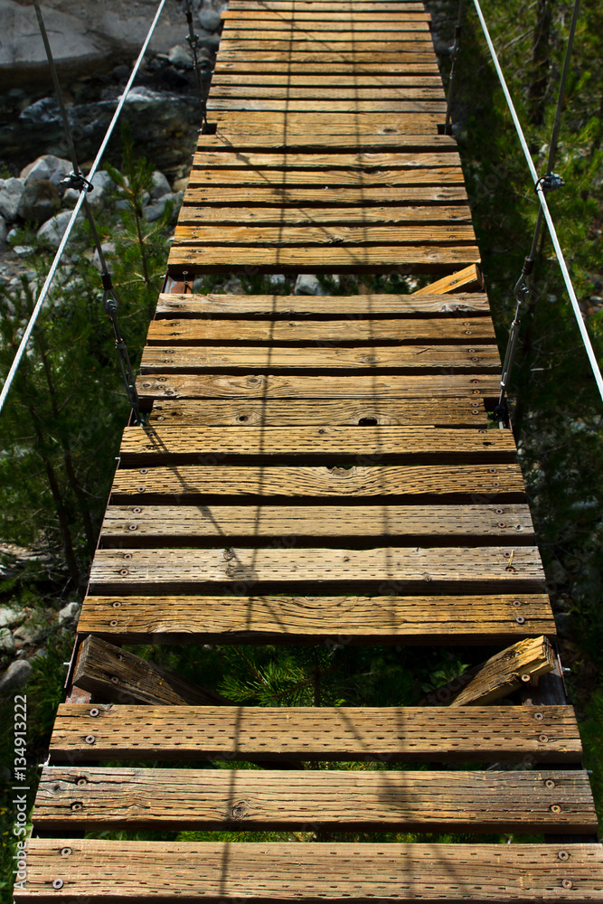 An old wooden suspension bridge with broken slats hangs over a river ...