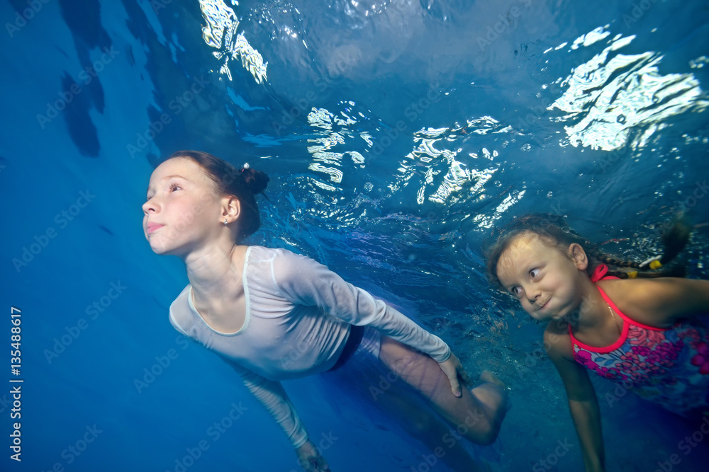 Two little girls swim underwater in the pool on a blue background ...