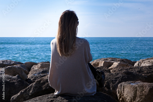 donna seduta di spalle sugli scogli guarda il mare - Acquista questa ...