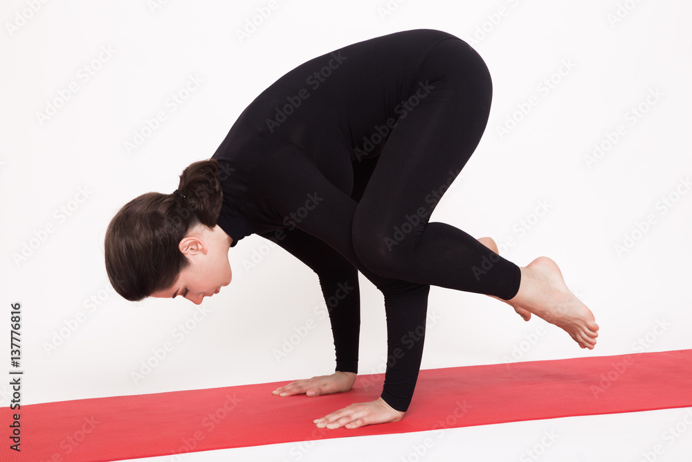 Beautiful athletic girl in a black suit doing yoga. Kakasana asana ...