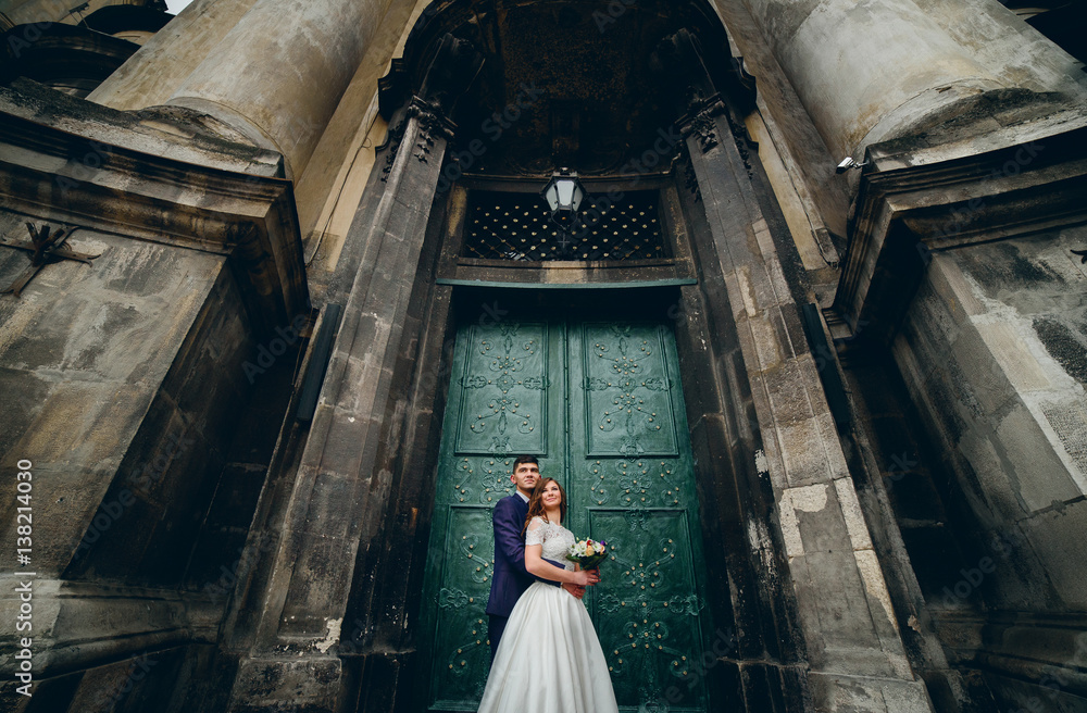 Tall groom hugs bride from behind standing with her before entrance to ...