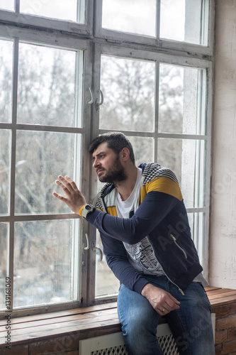 Emotional sad bearded man looking through the window. He is looking ...