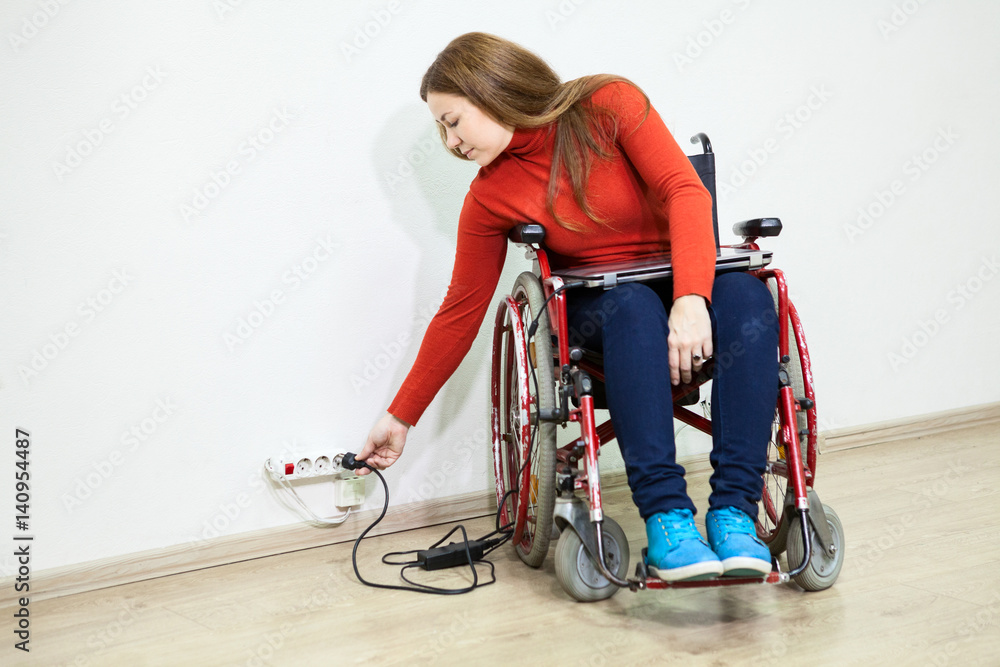 Disabled Caucasian woman in wheelchair stretching to power socket in ...