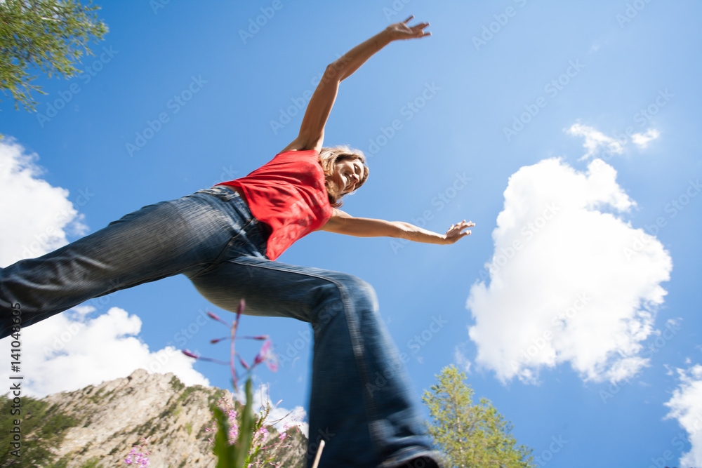 femme souriant en contre plongée qui saute dans les montagne en été ...