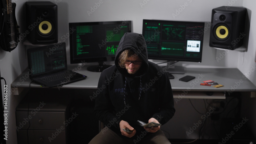 Hooded hacker in black clothes sitting on a chair in the room and ...
