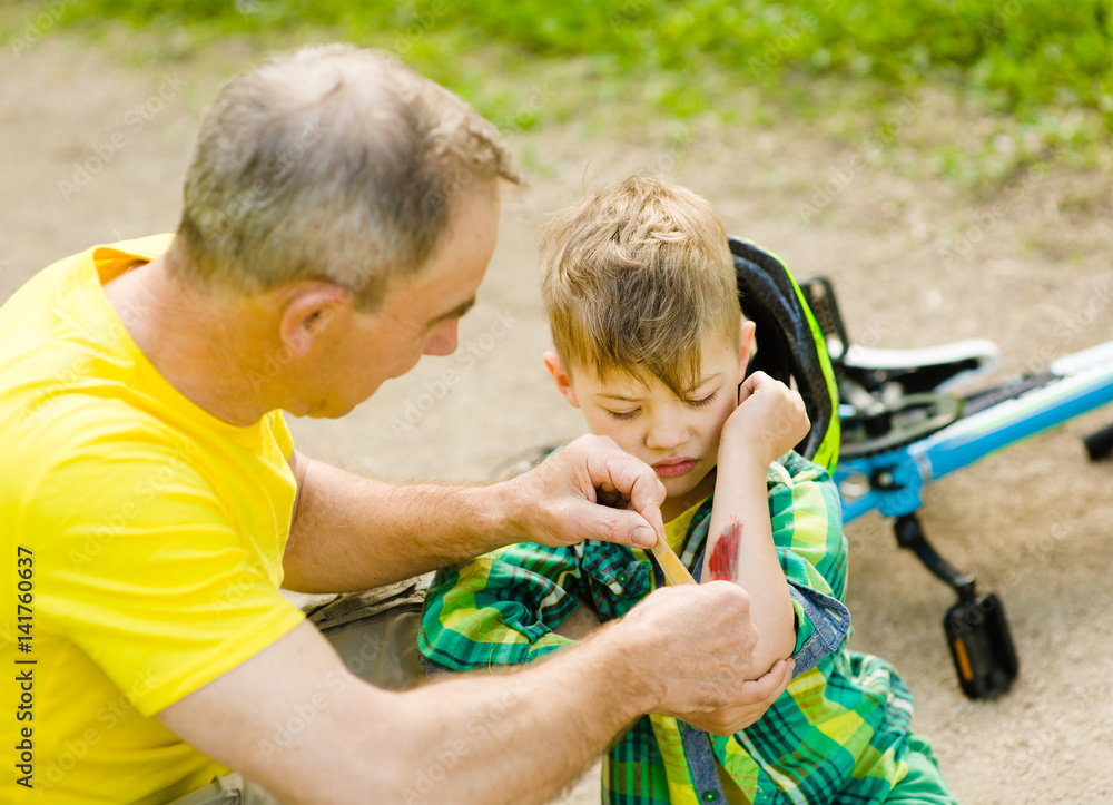 Grandfather putting band-aid on young boy's injury who fell off his ...