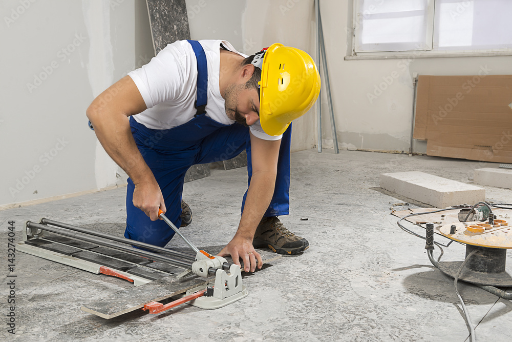 Construction worker wearing bib overalls and hard hat cutting ceramic ...