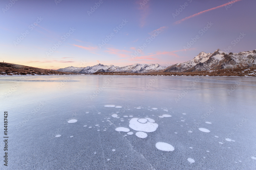 Ice bubbles on the frozen surface of Andossi Lake at sunrise Spluga ...