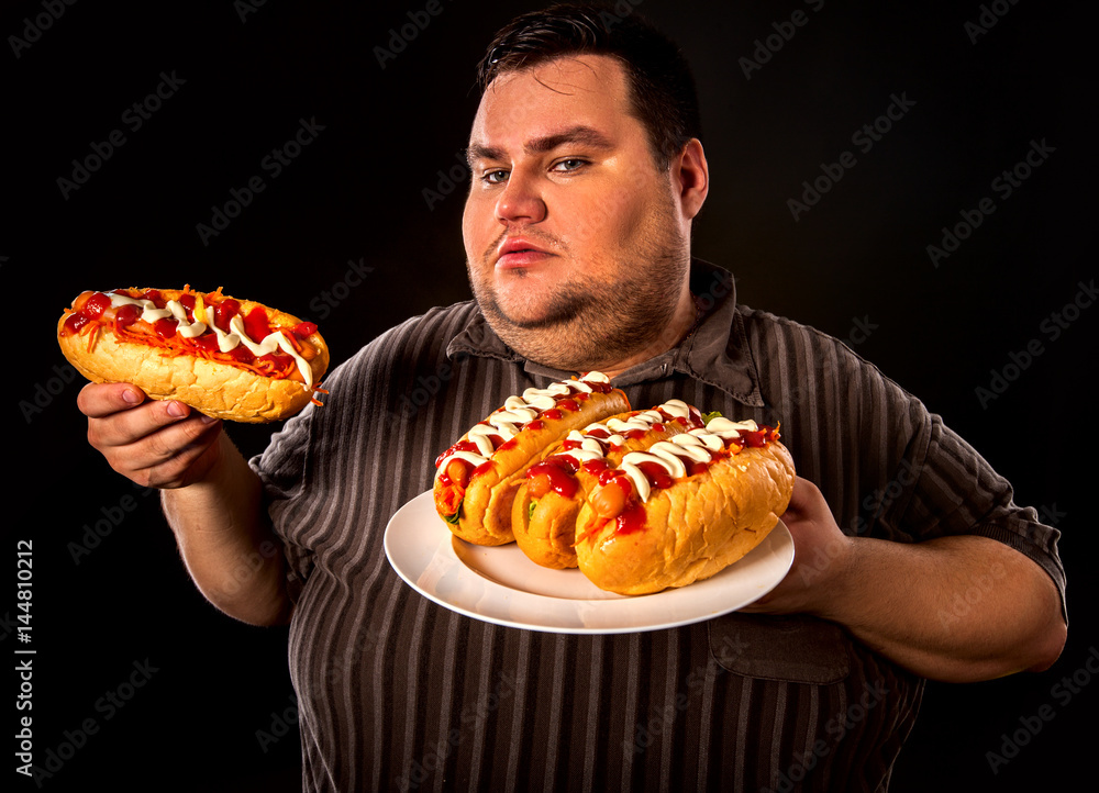 Fat man eating fast food hot dog on plate. Breakfast for overweight ...