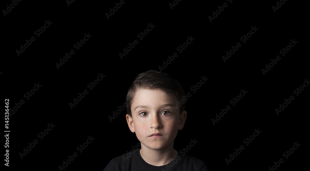 Low key portrait of young boy isolated on black background. Plenty of ...