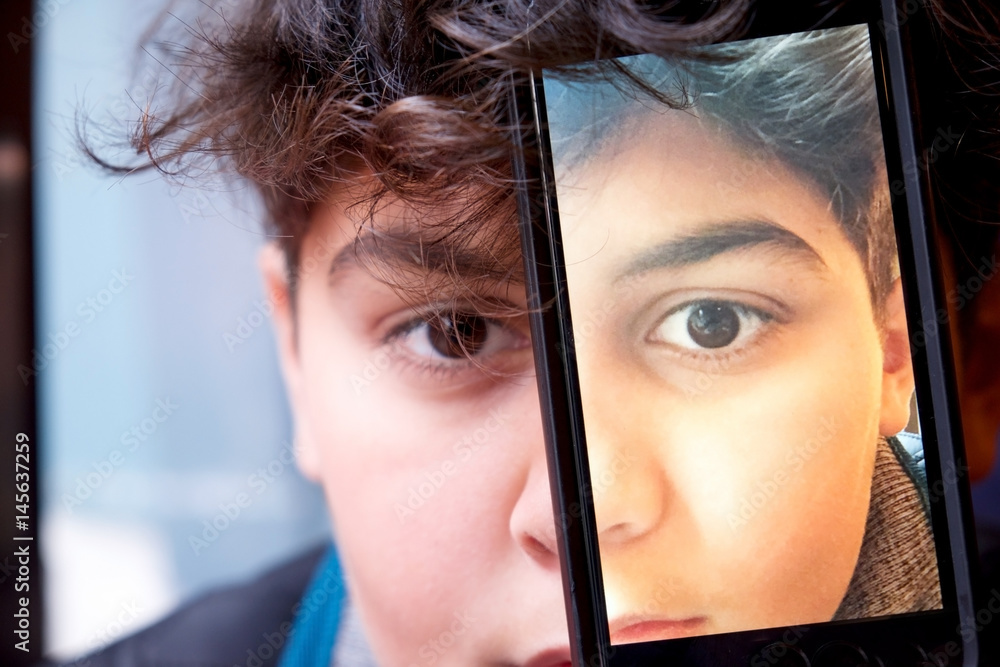 13 year old boys face close up with mobile phone covering one half of ...