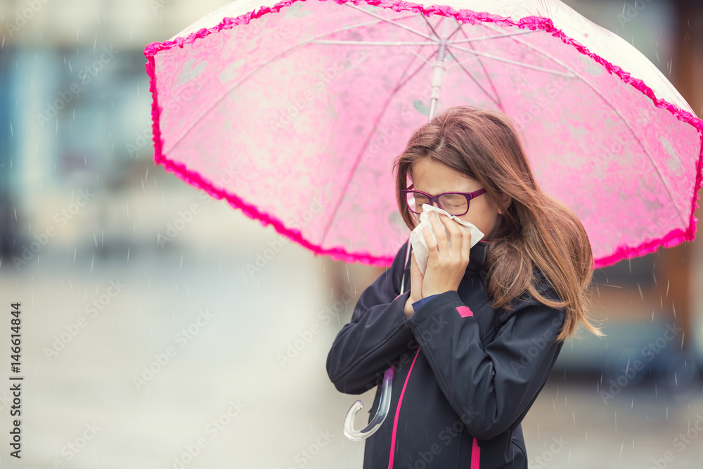 Foto Young girl with flu blowing her nose with a tissue paper under ...