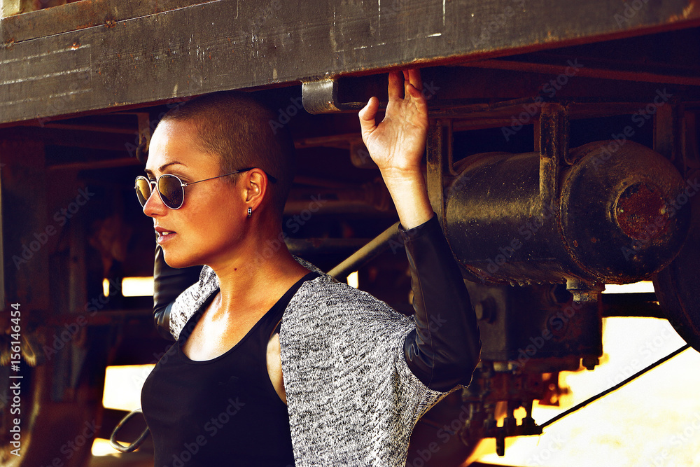 Shaved headed girl in black sun glasses and brown bronzed skin profile ...
