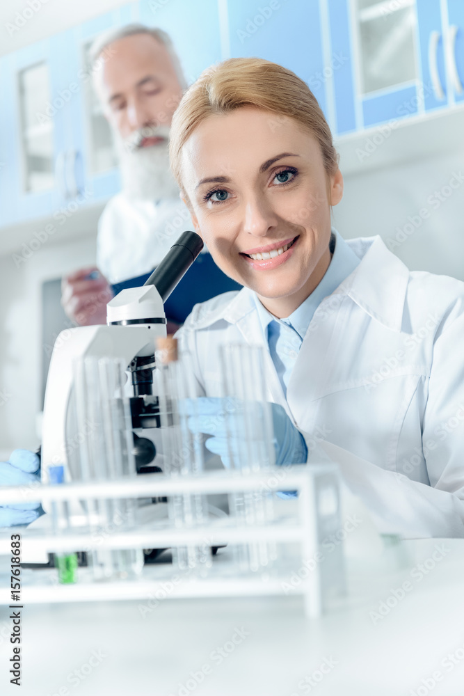 caucasian smiling scientist in white coat working with microscope and ...