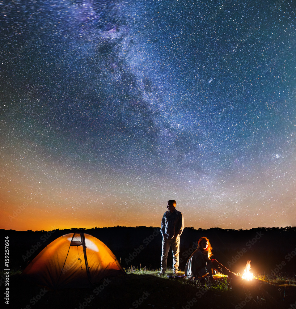 Romantic couple hikers in his camp at night near campfire and tent ...