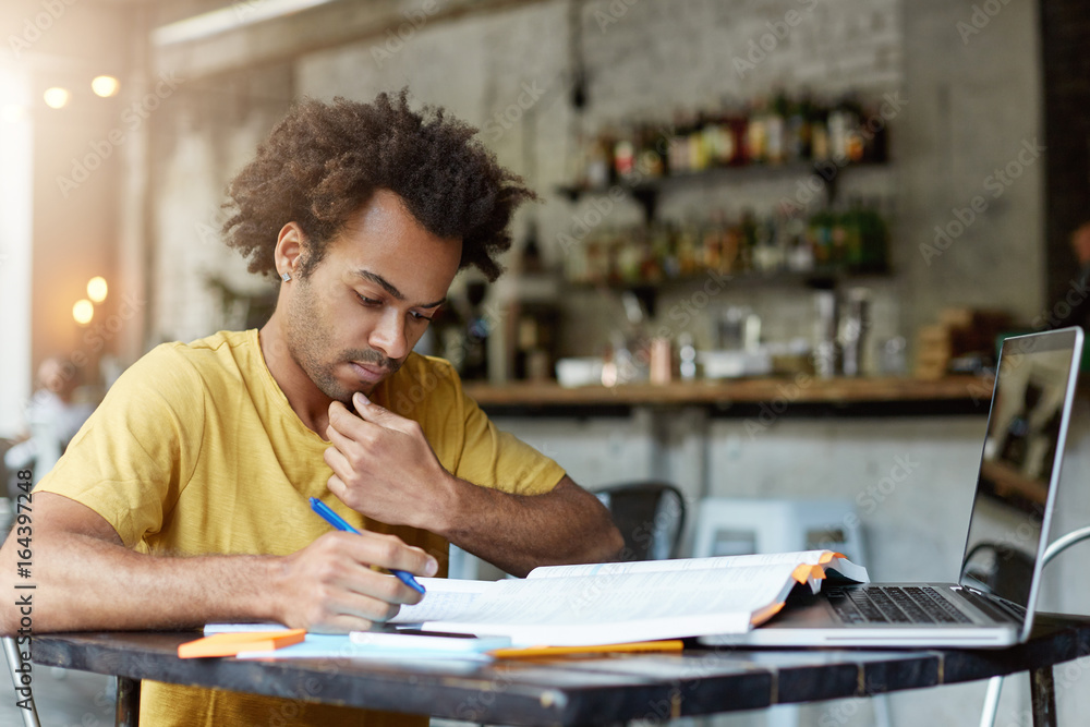 Solemn dark-skinned African American student at his workplace looking ...