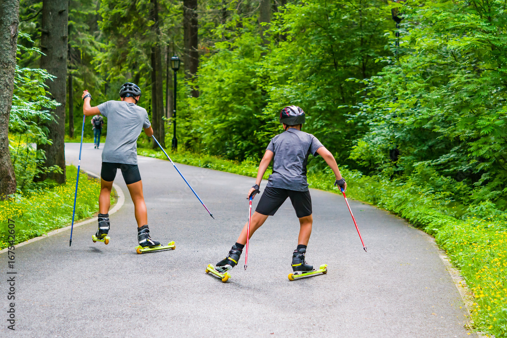Boys teens ride in the forest along the asphalt road on roller skis ...