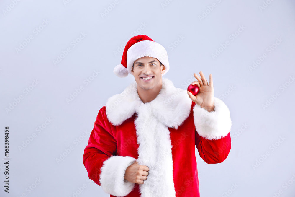 Handsome man in Santa Claus costume holding shiny bauble on light ...
