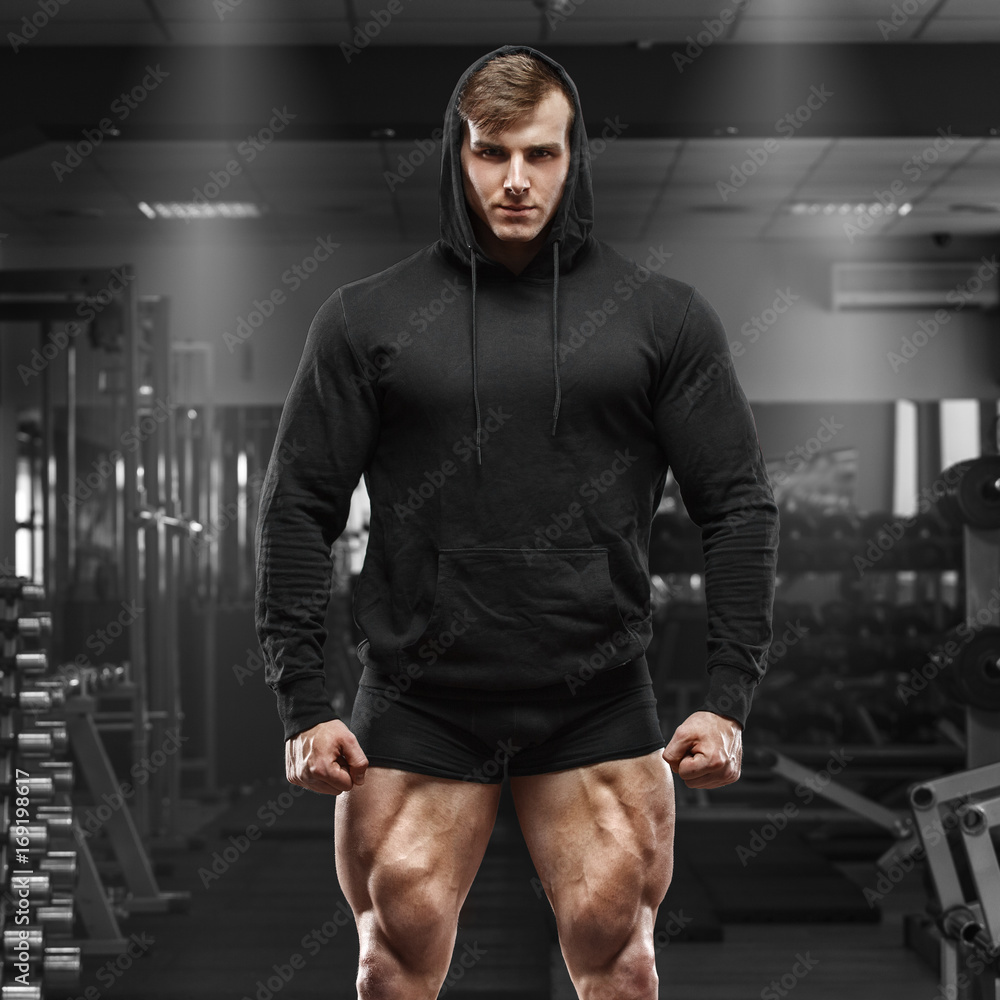 Muscular man with muscle legs in gym. Strong male in black hoodie with ...