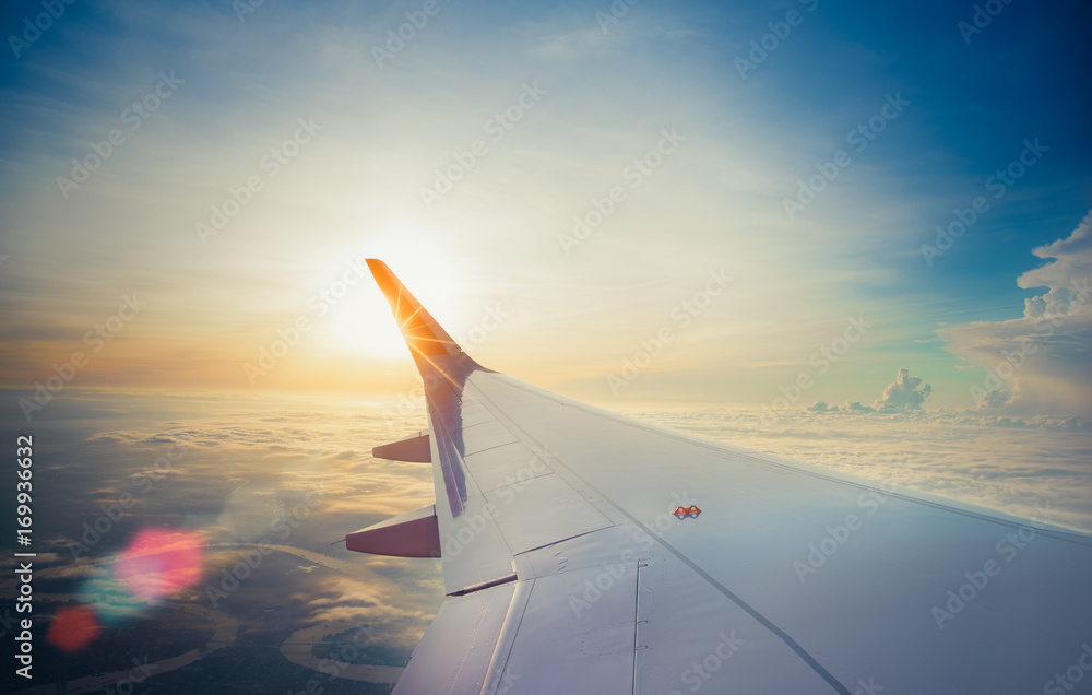 Wing of airplane flying above the clouds in the sunset sky background ...