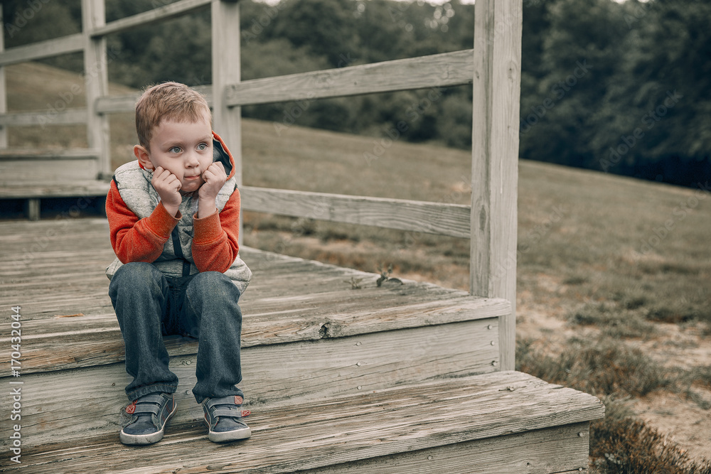 pensive boy sitting on wooden steps. child patiently waiting on the ...