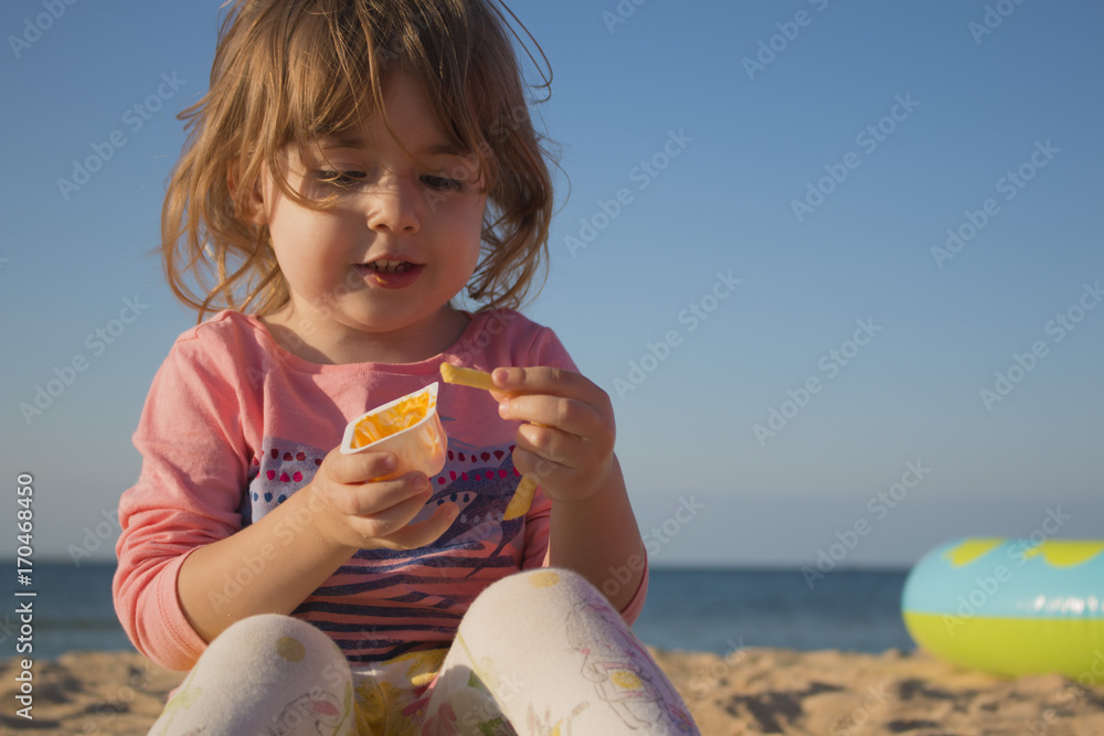 very pretty girl eating french fry and sauce. girl sitting on the sand ...