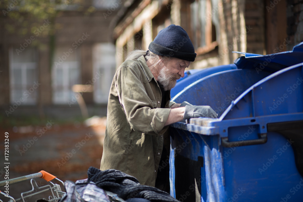 Beardy homeless man searching for empty bottles in trash can. Living in ...