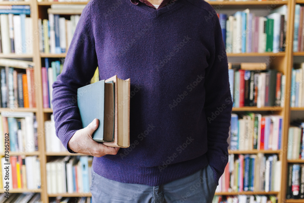 A man holding books under his arm, standing in front of a bookcase ...