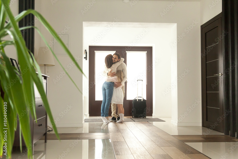 Woman and little girl embracing man standing in hall, wife meeting ...