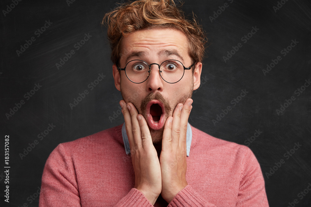 Stupefied shocked surprised young male has trendy hairstyle, looks with ...
