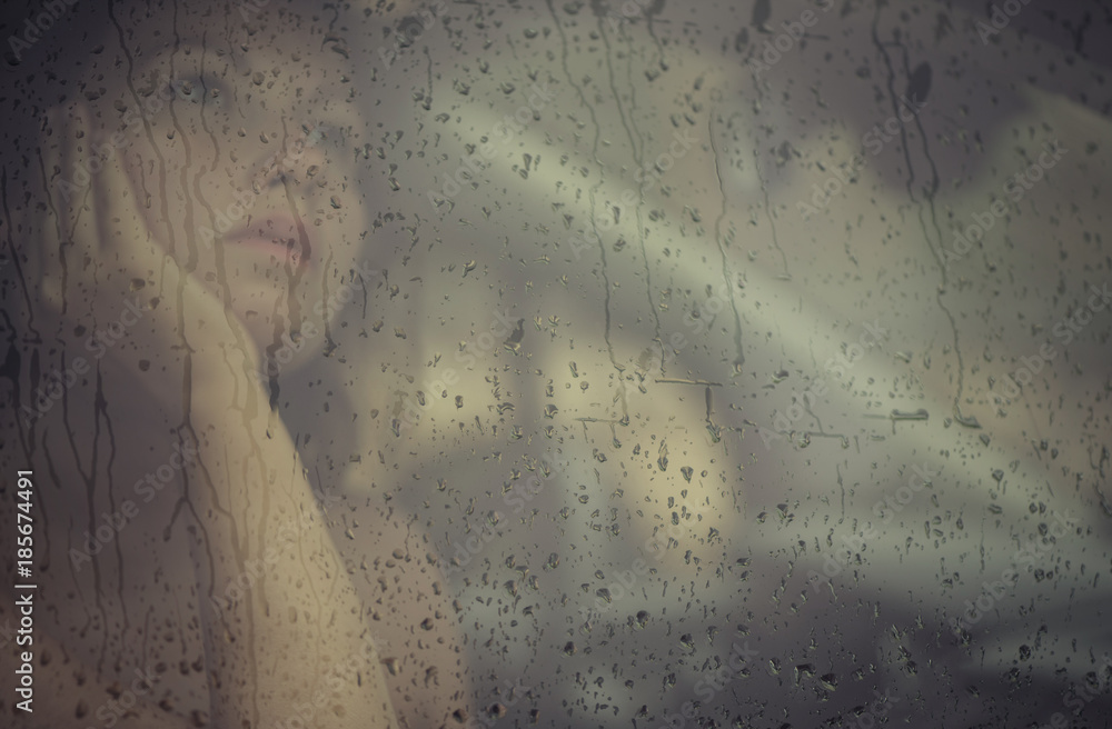 Sad woman looking through the window with rain drop in the car. Face of ...