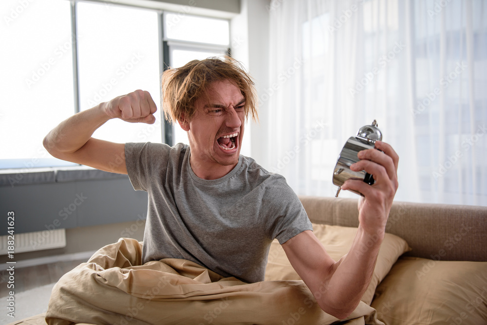Feeling furious. Waist up portrait of angry guy sitting in bed in the ...
