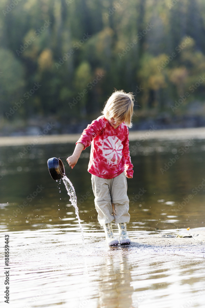 Boy pouring water out of kettle into river Stock Photo | Adobe Stock